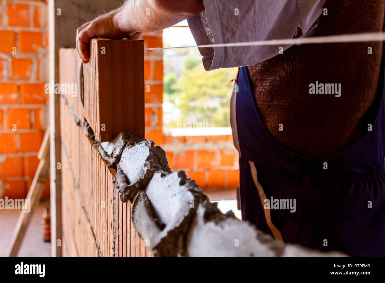 Mason, bricklayer worker is using red blocks to mount a wall next the ...