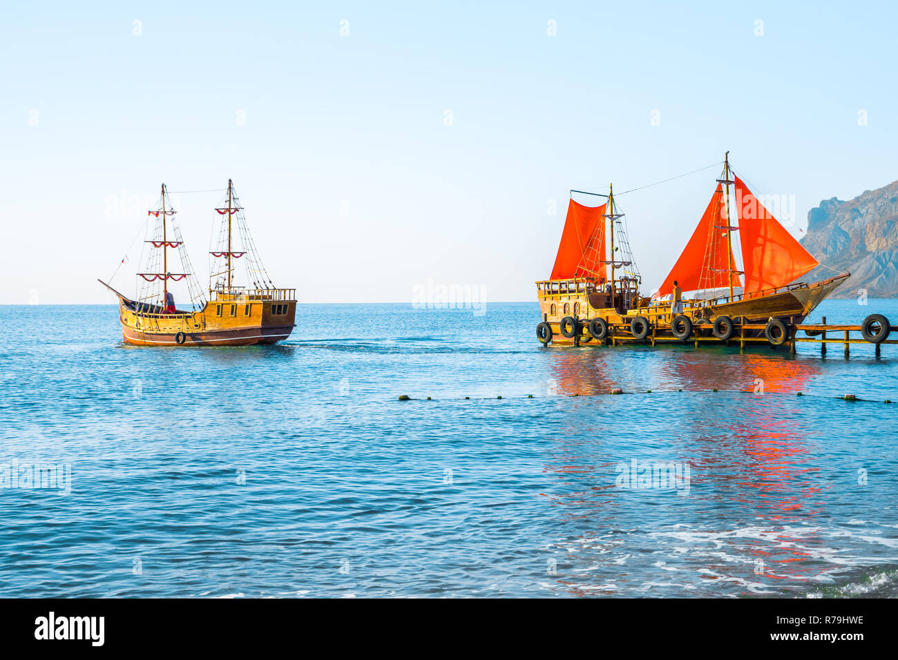 Two old wooden ships. One of them with red sails is on the pier Stock ...