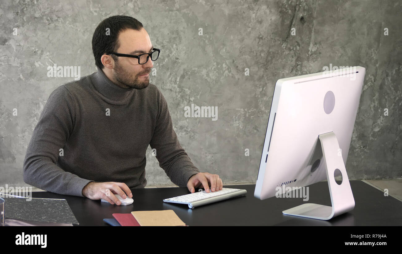 Casual businessman working in office, sitting at desk, typing on ...