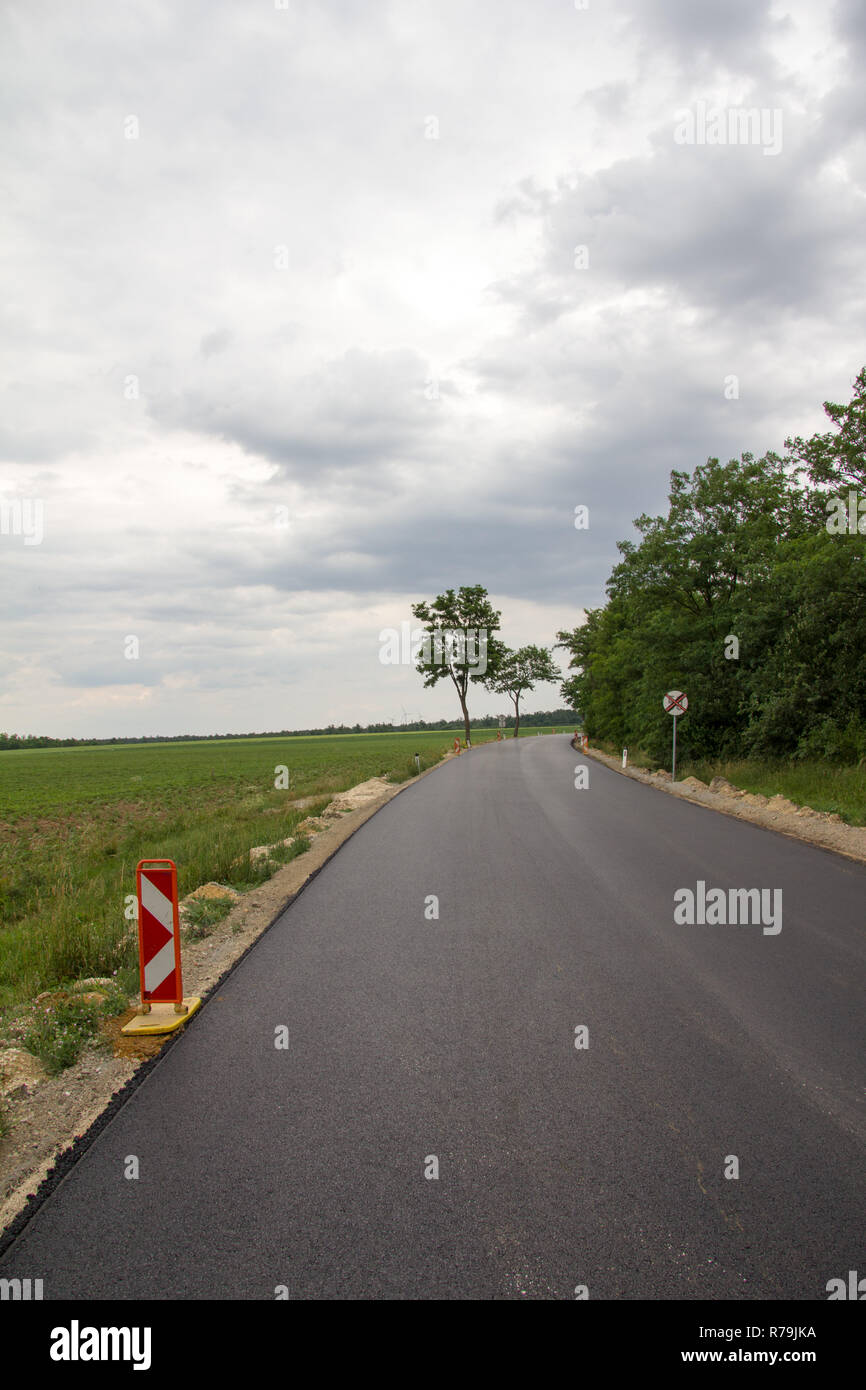 freshly asphalted road in the flat country with cloudy sky in early ...