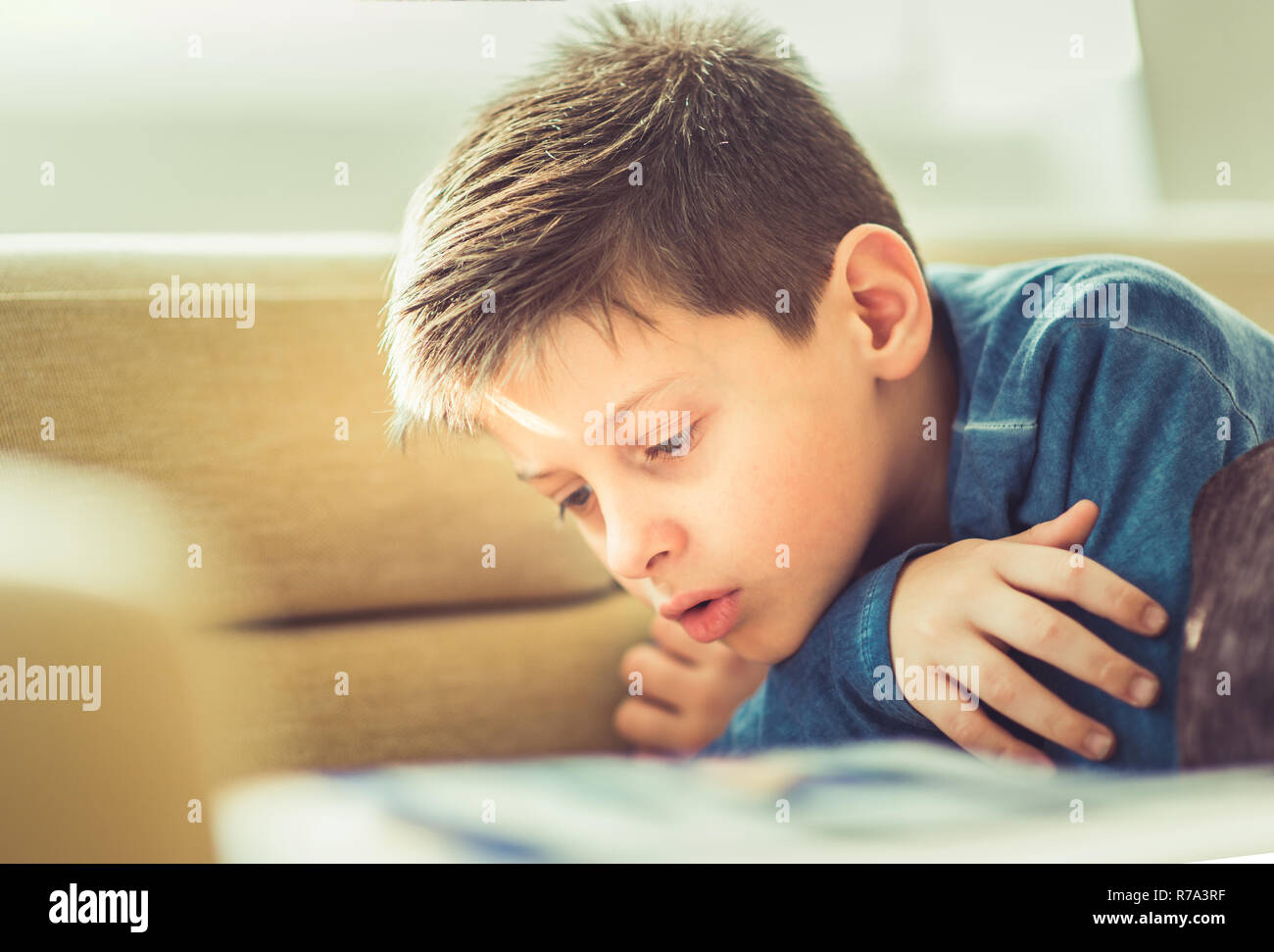 A beautiful kid is in the living room, lying and reading a book Stock ...