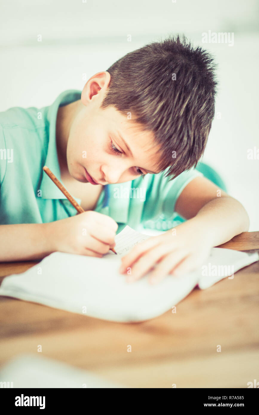 A little kid is sitting on the table and writing in his notebook Stock ...
