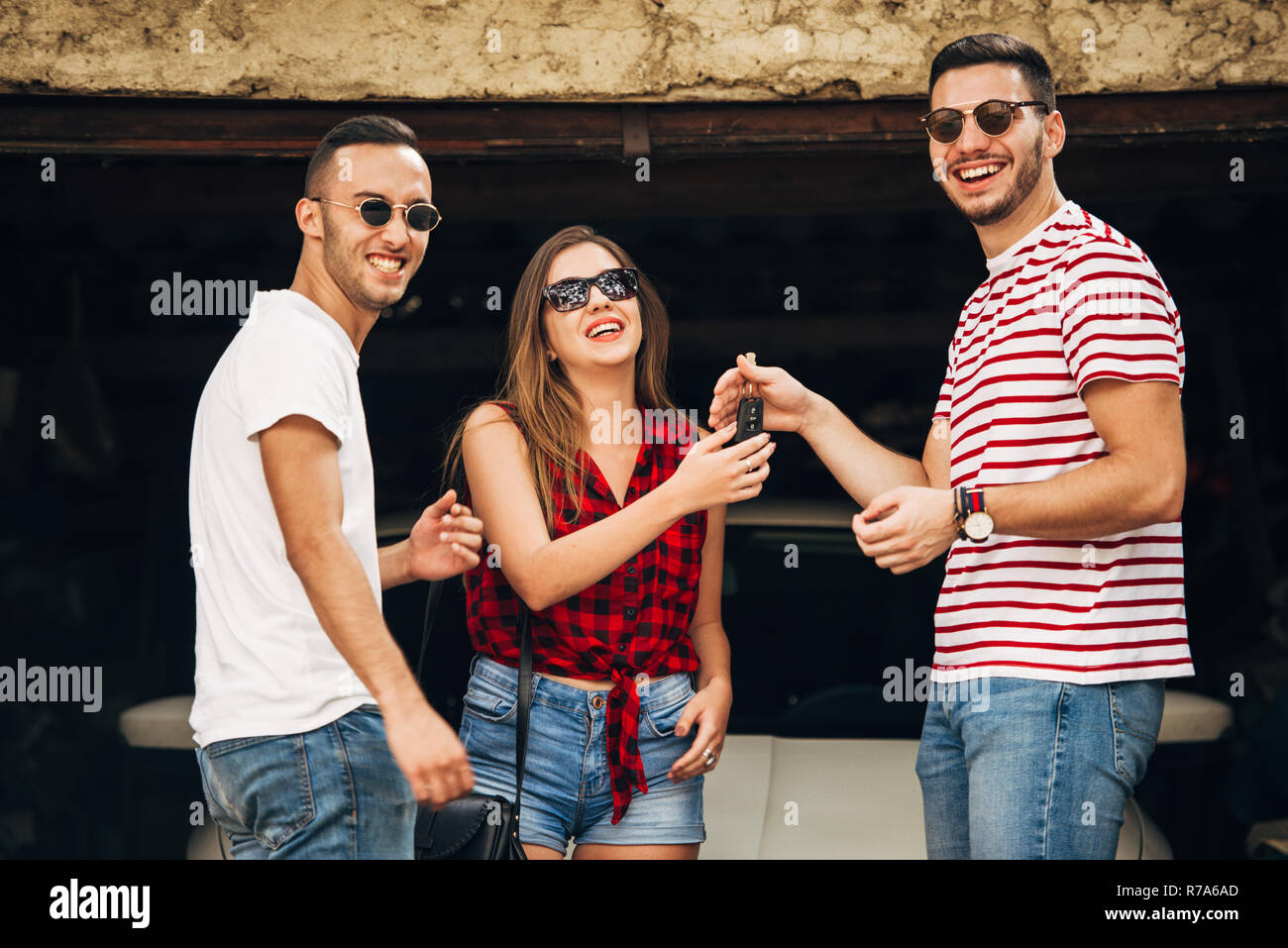 Group of smiling friends exchange car keys on the front from car garage ...