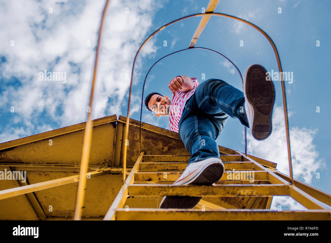 Courage man climbing on metal stairs, looking down, above blue sky ...