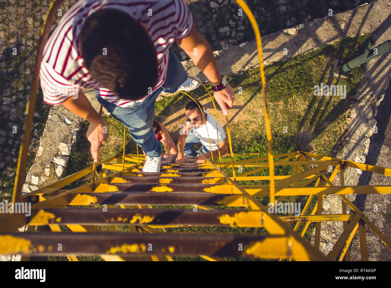 Man going front on high ladder while his two friends are on the bottom ...