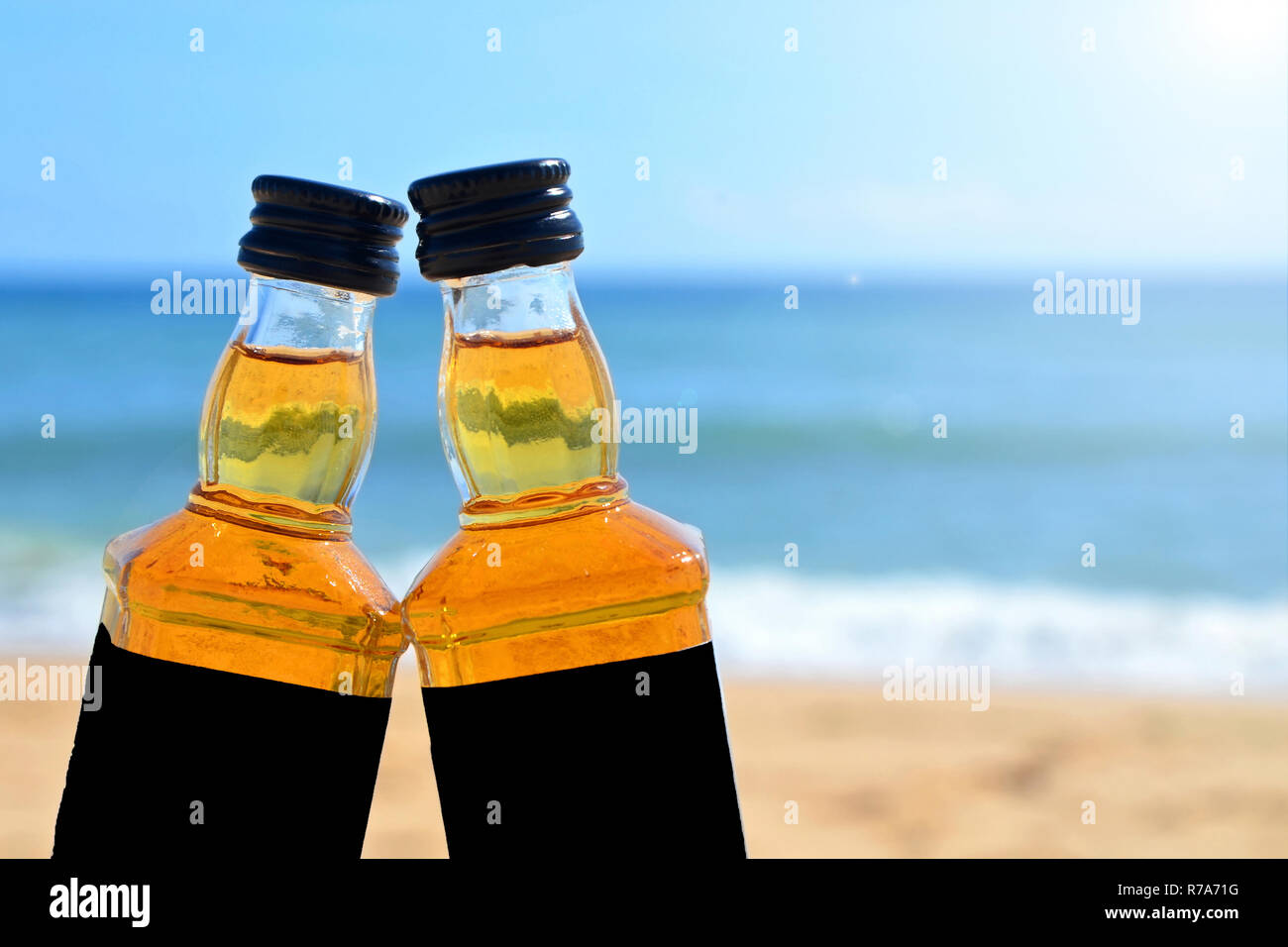 Two little bottles whiskey stand on the sand closeup. Alcoholic party ...