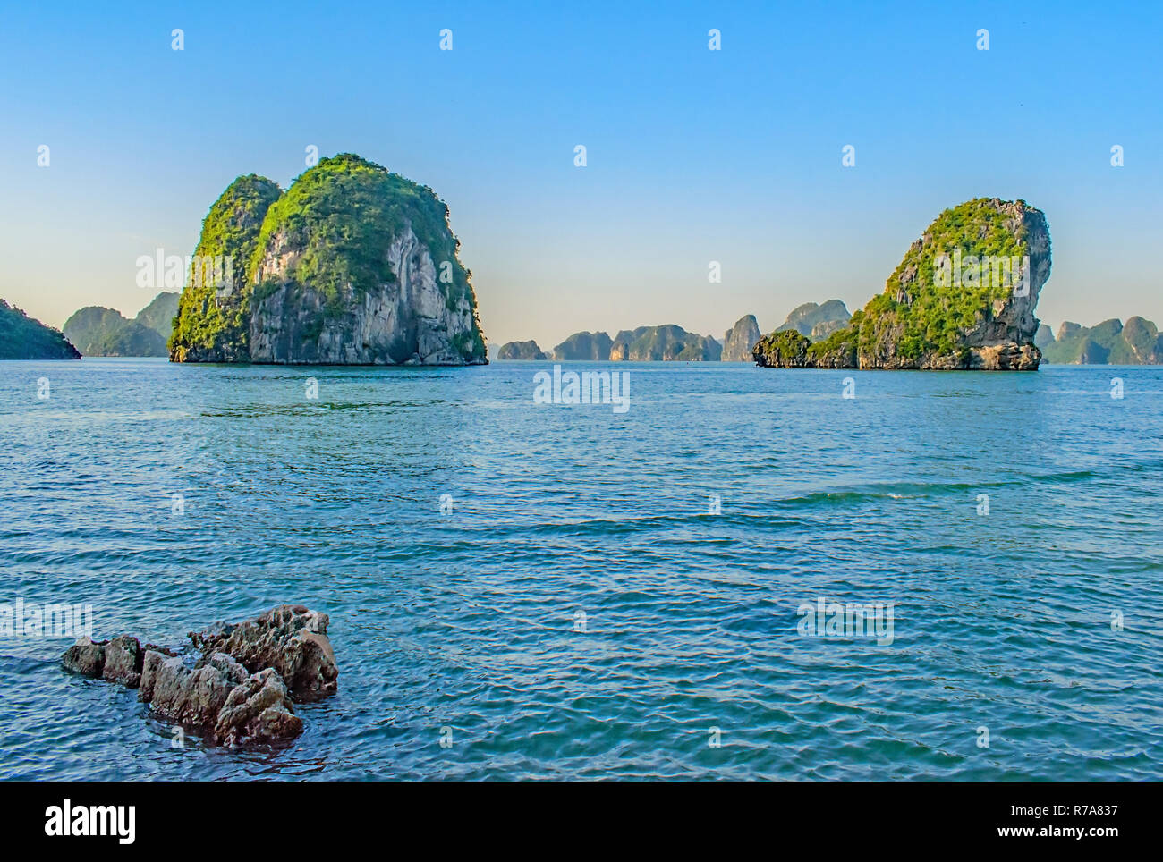 An eroded sloping limestone karst sits in the blue water of Halong Bay ...