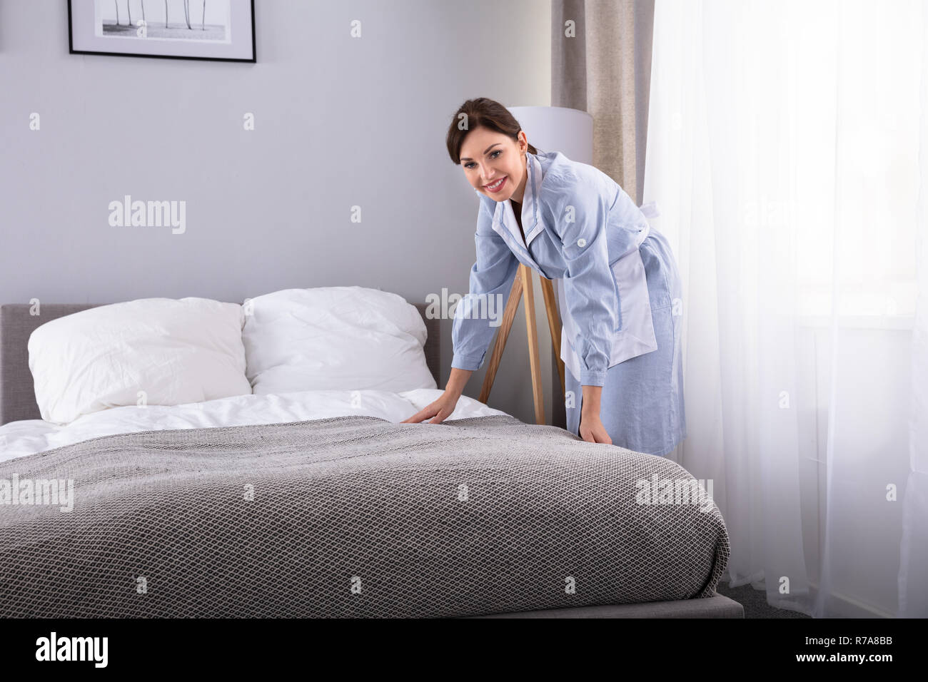 Smiling Female Housekeeper Making Bed In Hotel Room Stock Photo - Alamy