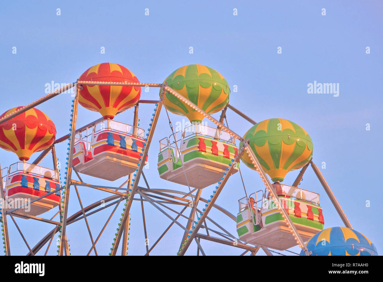 Multicolored booths of a ferris wheel over a blue sky background with a ...