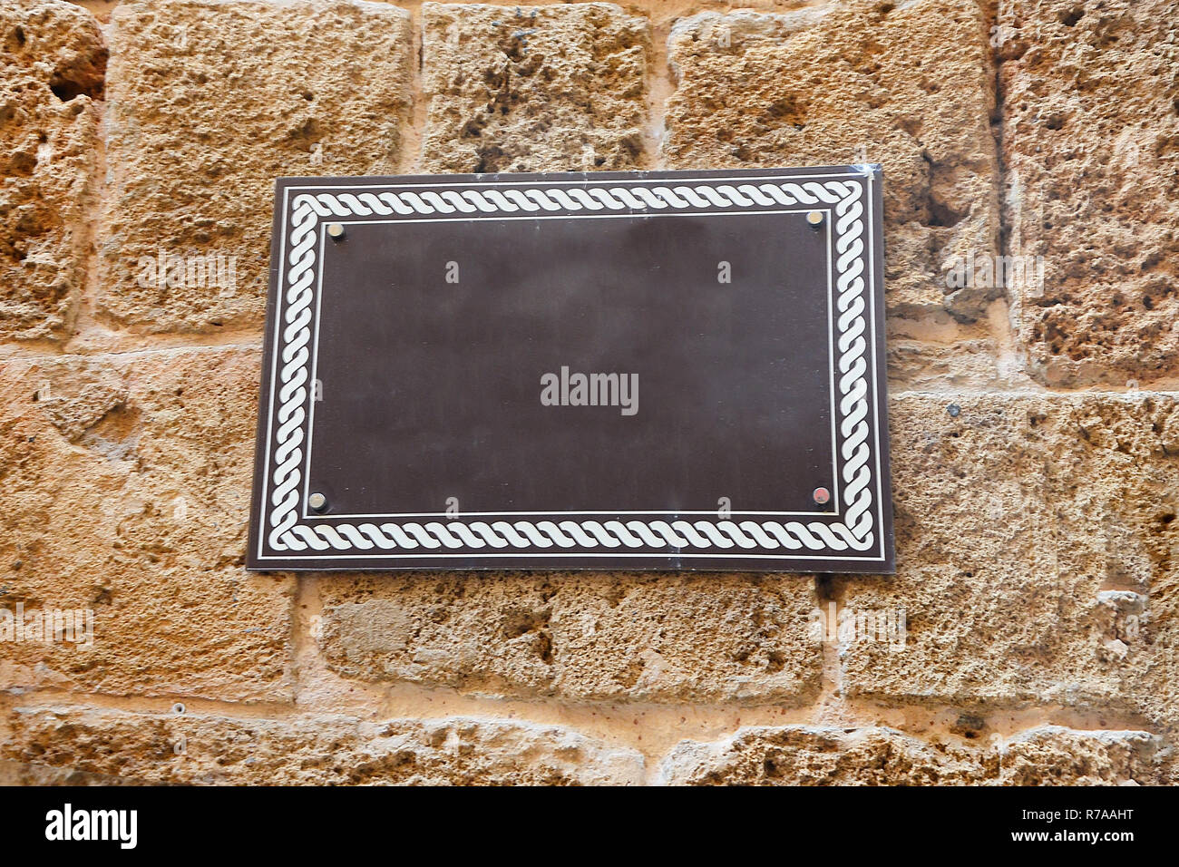 A brown sign with a white frame hangs on a stone wall Stock Photo - Alamy