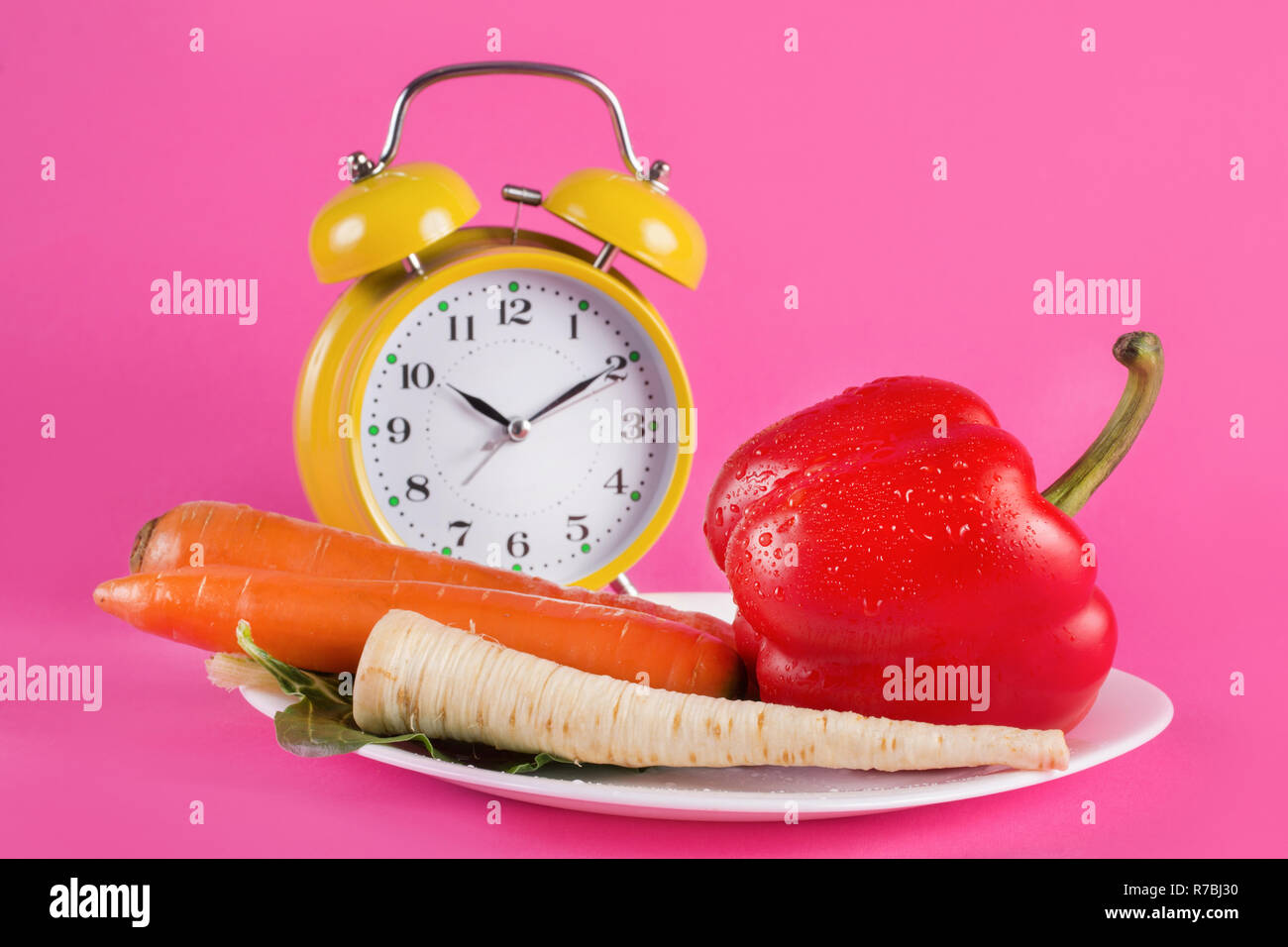 Vegetables on a plate and retro alarm clock isolated on pink background ...