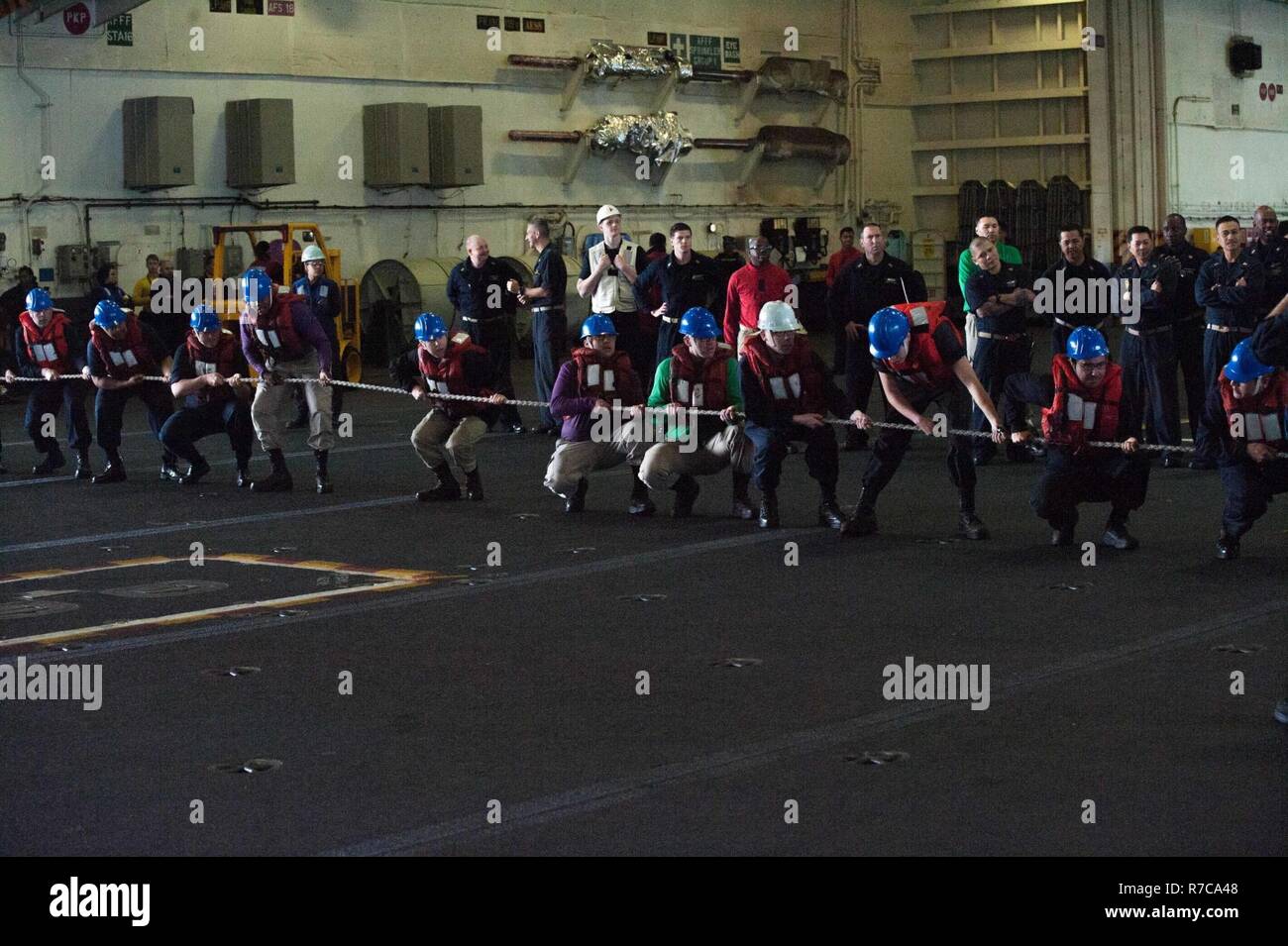 Senior enlisted Sailors haul in a messenger line in the hangar bay. The ...