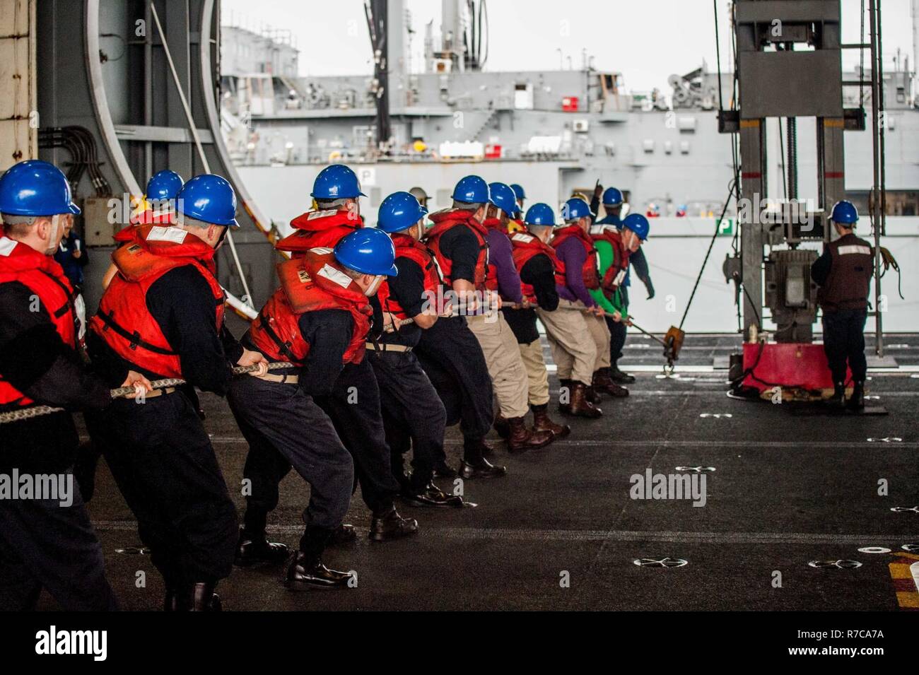 Senior enlisted Sailors haul in a messenger line in the hangar bay. The ...