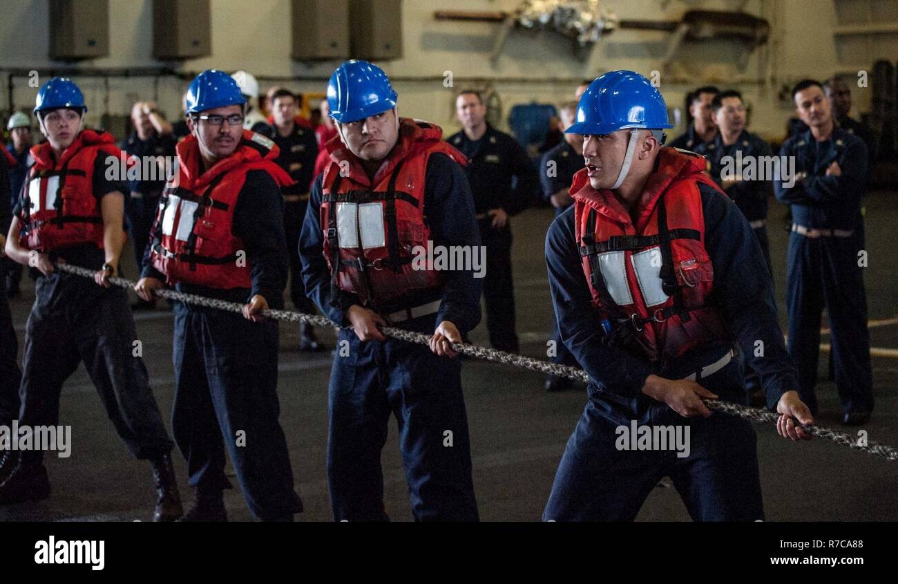 Senior enlisted Sailors haul in a messenger line in the hangar bay. The ...