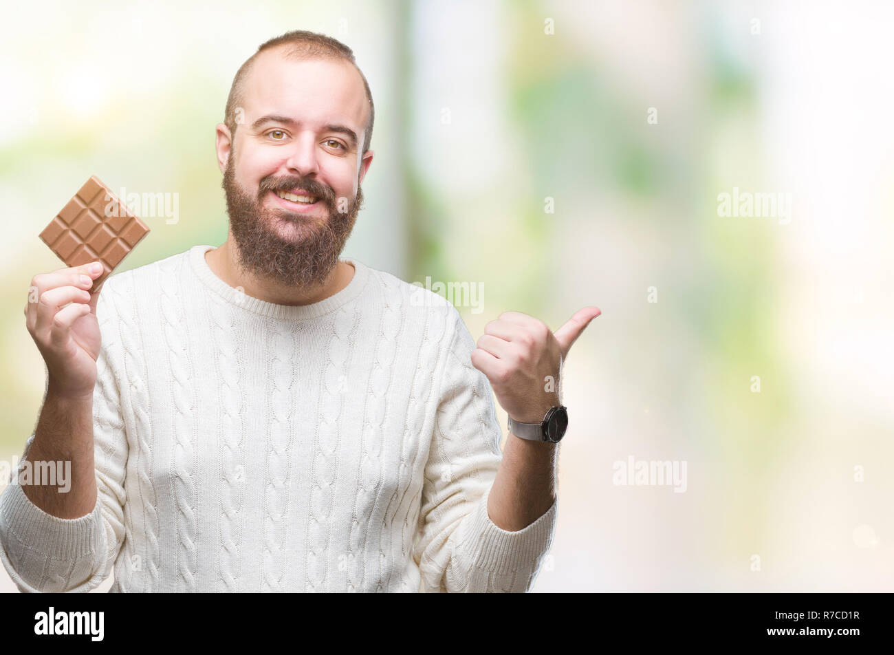 Young hipster man eating chocolate bar over isolated background ...