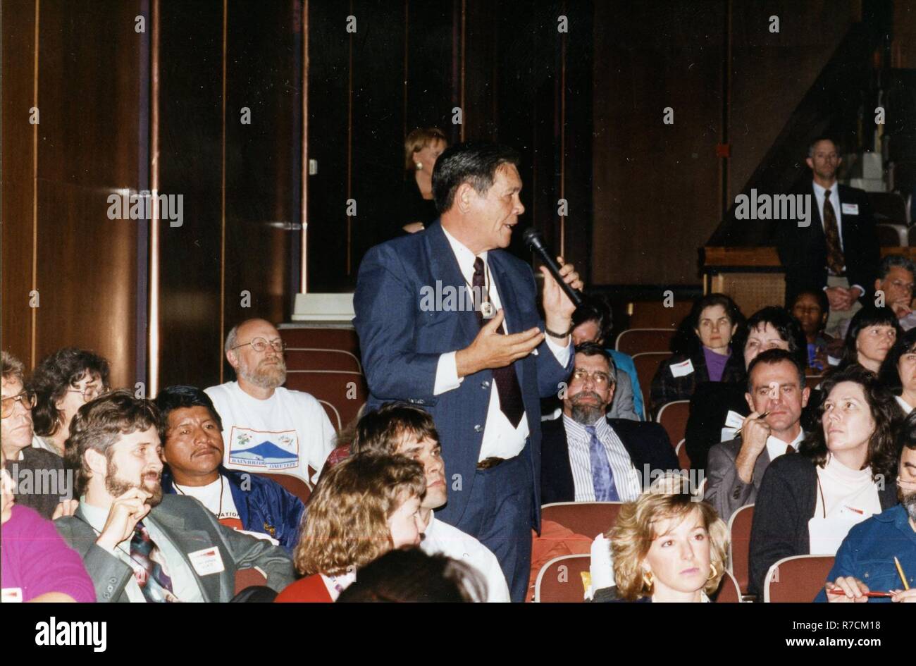 A MAN STANDING UP TALKING IN THE MIC TO A GROUP OF MEN AND WOMEN Stock ...