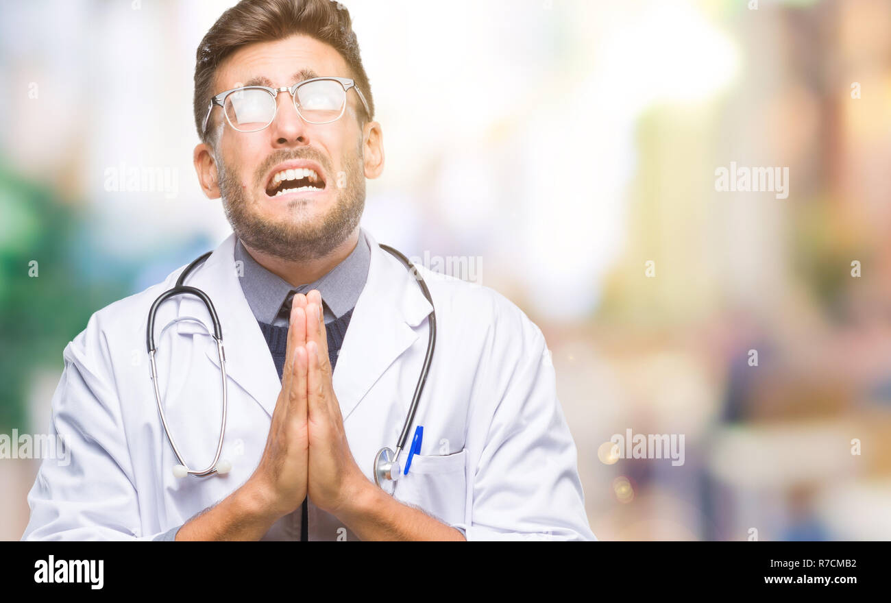 Young handsome doctor man over isolated background begging and praying ...