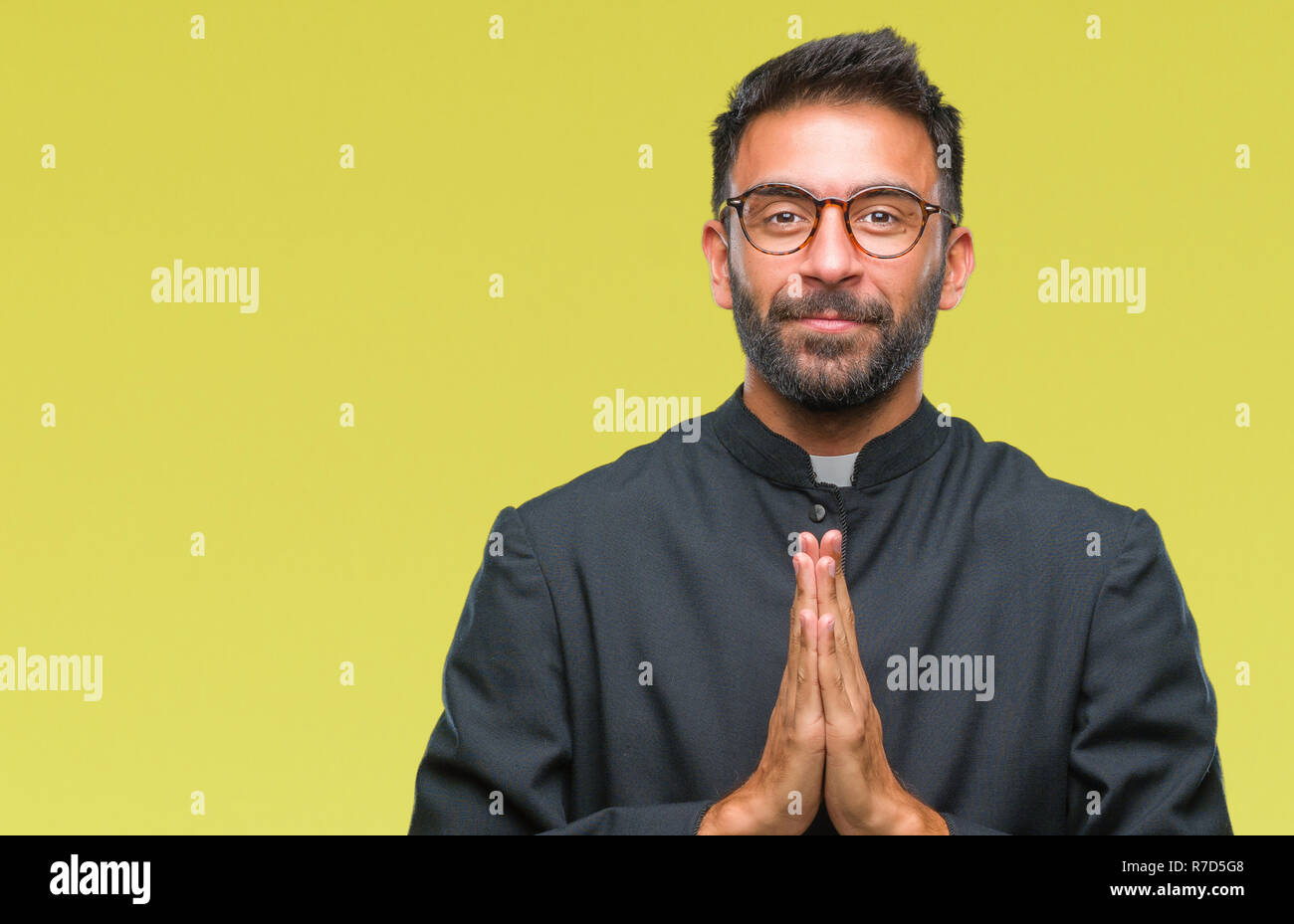 Adult hispanic catholic priest man over isolated background praying ...