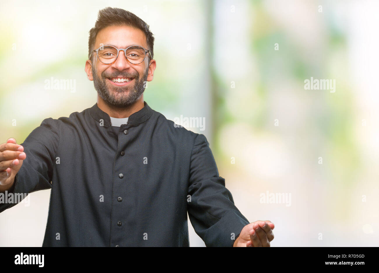 Adult hispanic catholic priest man over isolated background looking at ...