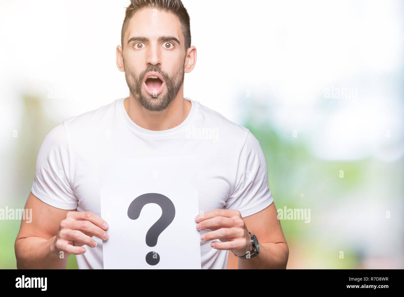Handsome young man holding paper with question mark over isolated ...