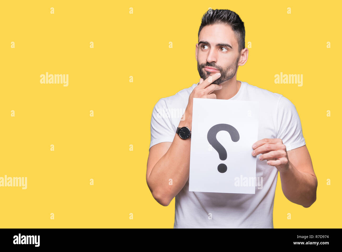 Handsome young man holding paper with question mark over isolated ...