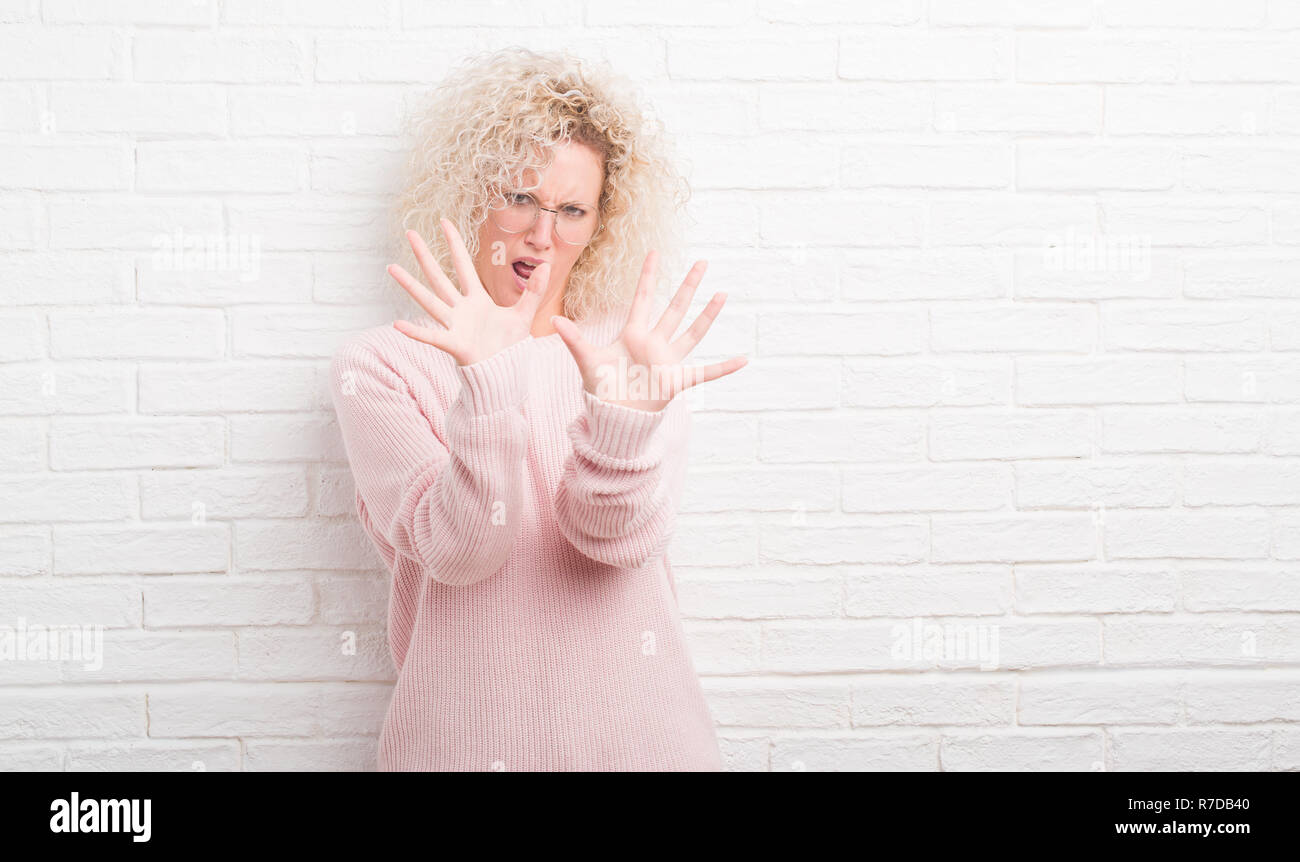 Young blonde woman with curly hair over white brick wall afraid and ...