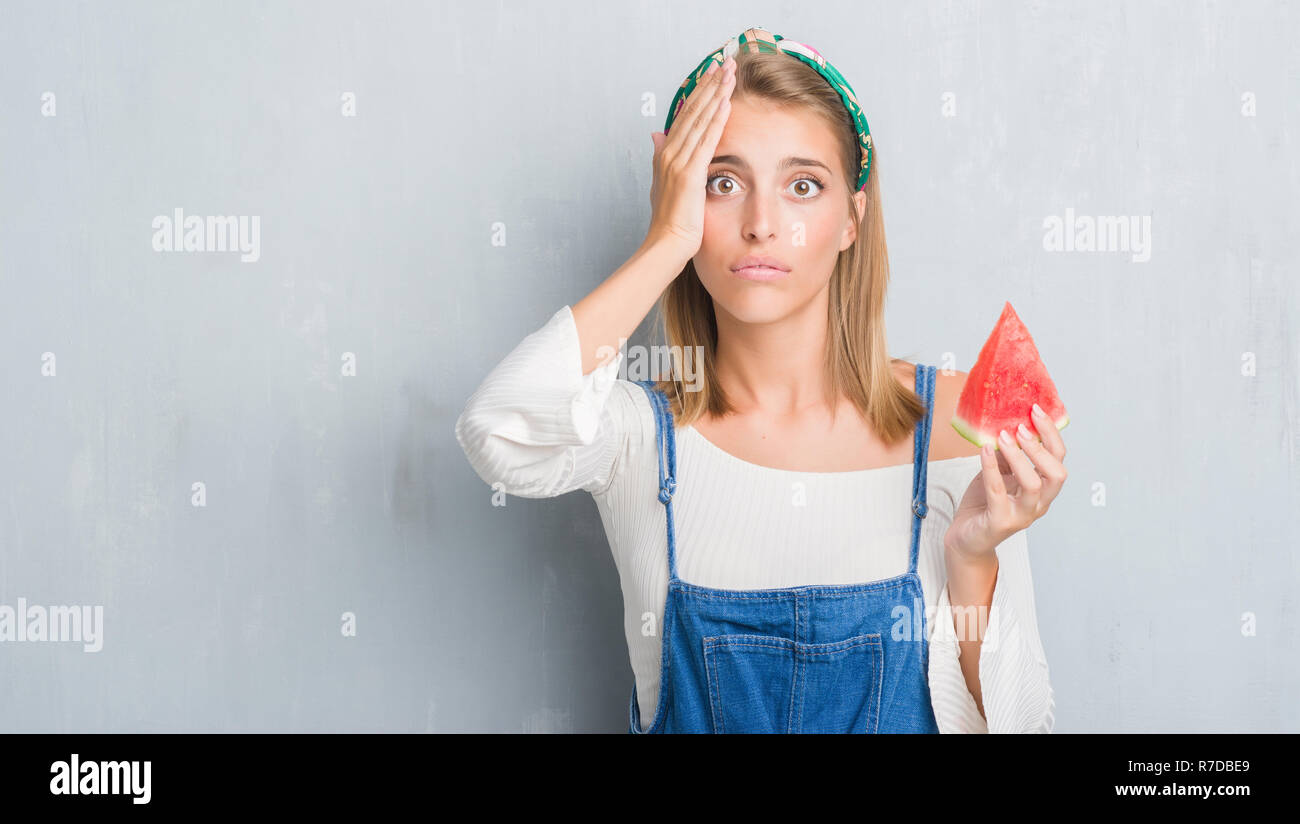 Beautiful young woman over grunge grey wall eating water melon stressed ...