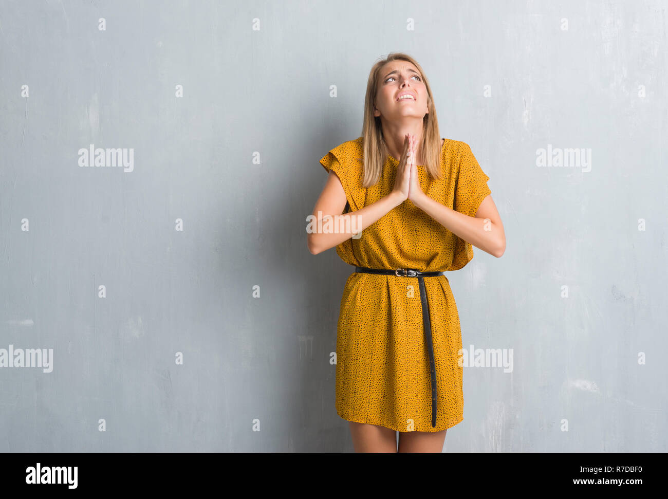 Beautiful young woman standing over grunge grey wall wearing a dress ...