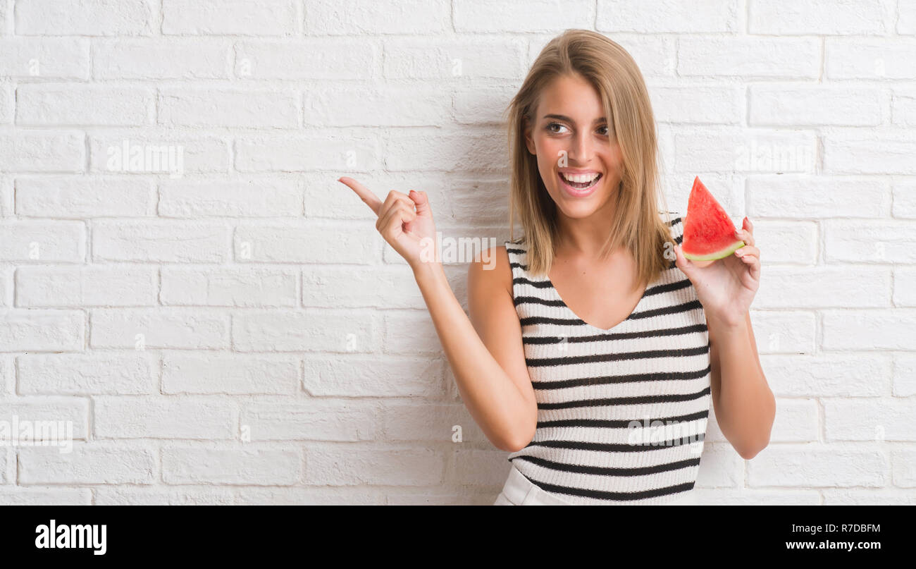 Beautiful young woman over white brick wall eating water melon slice ...