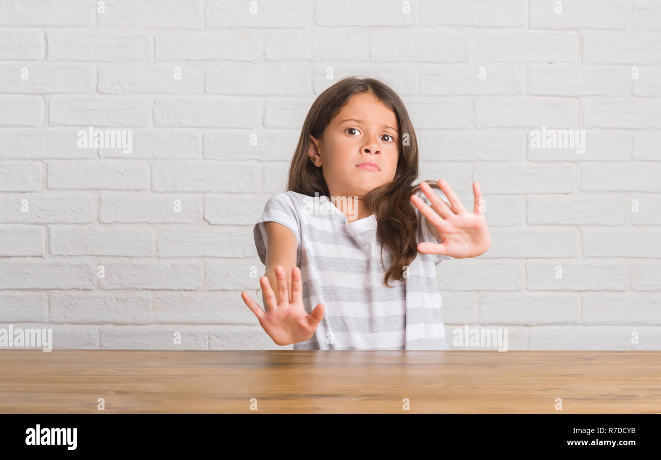 Young hispanic kid sitting on the table at home afraid and terrified ...