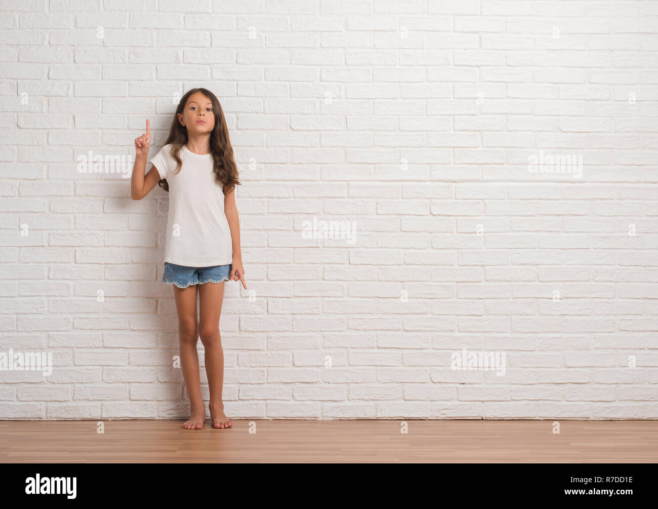 Young hispanic kid stading over white brick wall showing and pointing ...