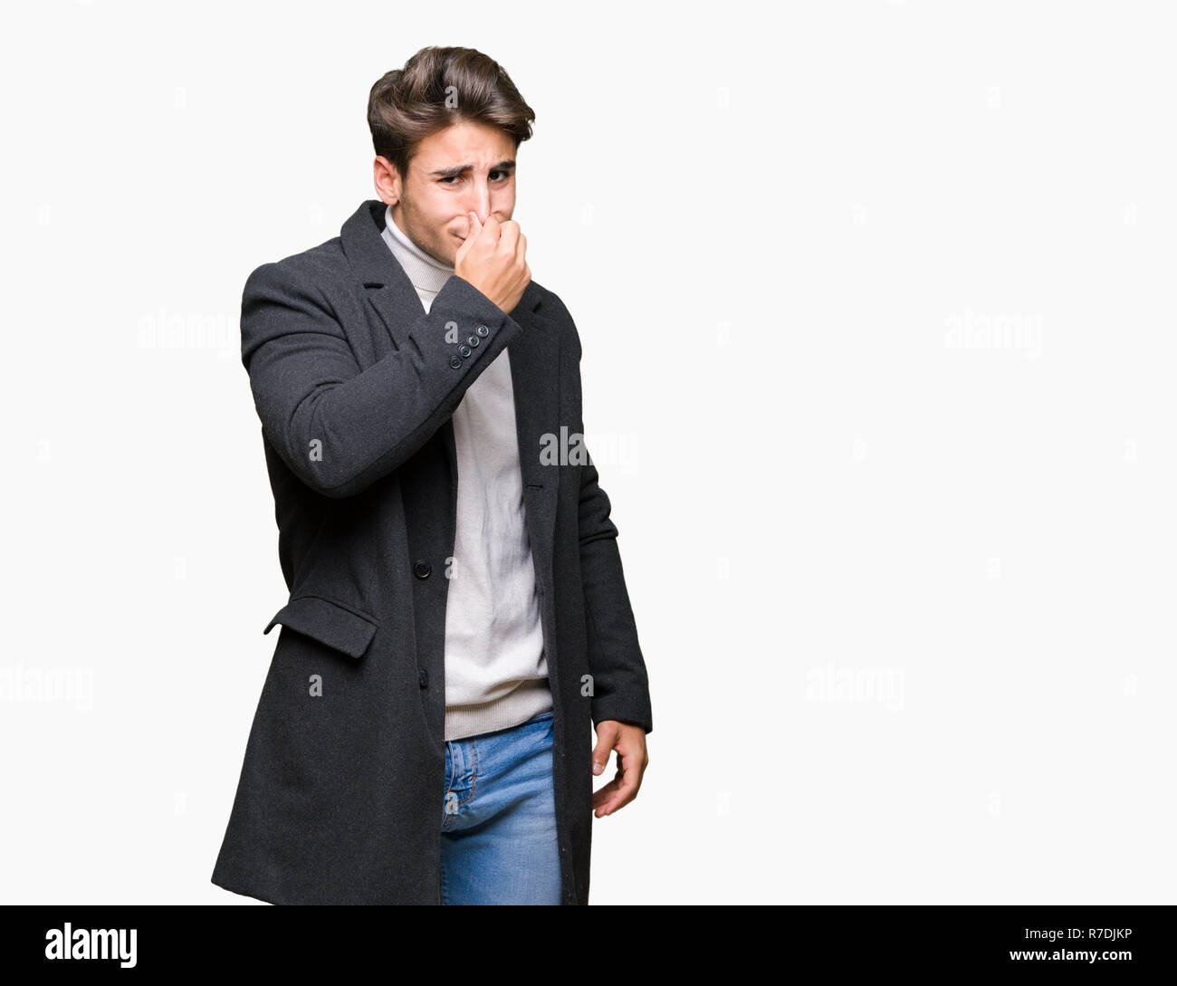 Young elegant man wearing winter coat over isolated background smelling ...