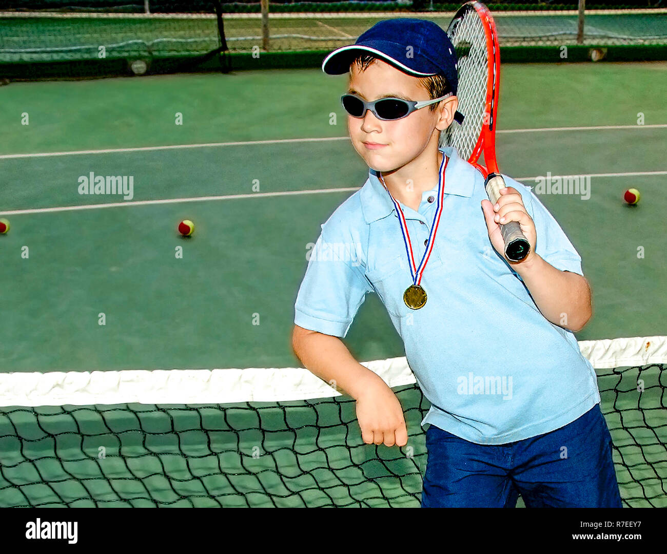 Little boy with hat and racket in his shoulder after a night tennis ...