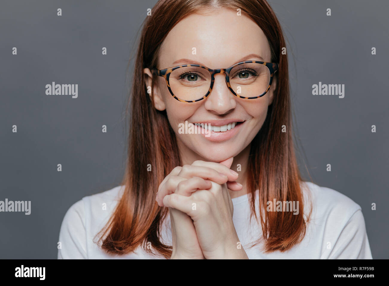 Close up shot of happy young European woman has pleasant smile, keeps ...