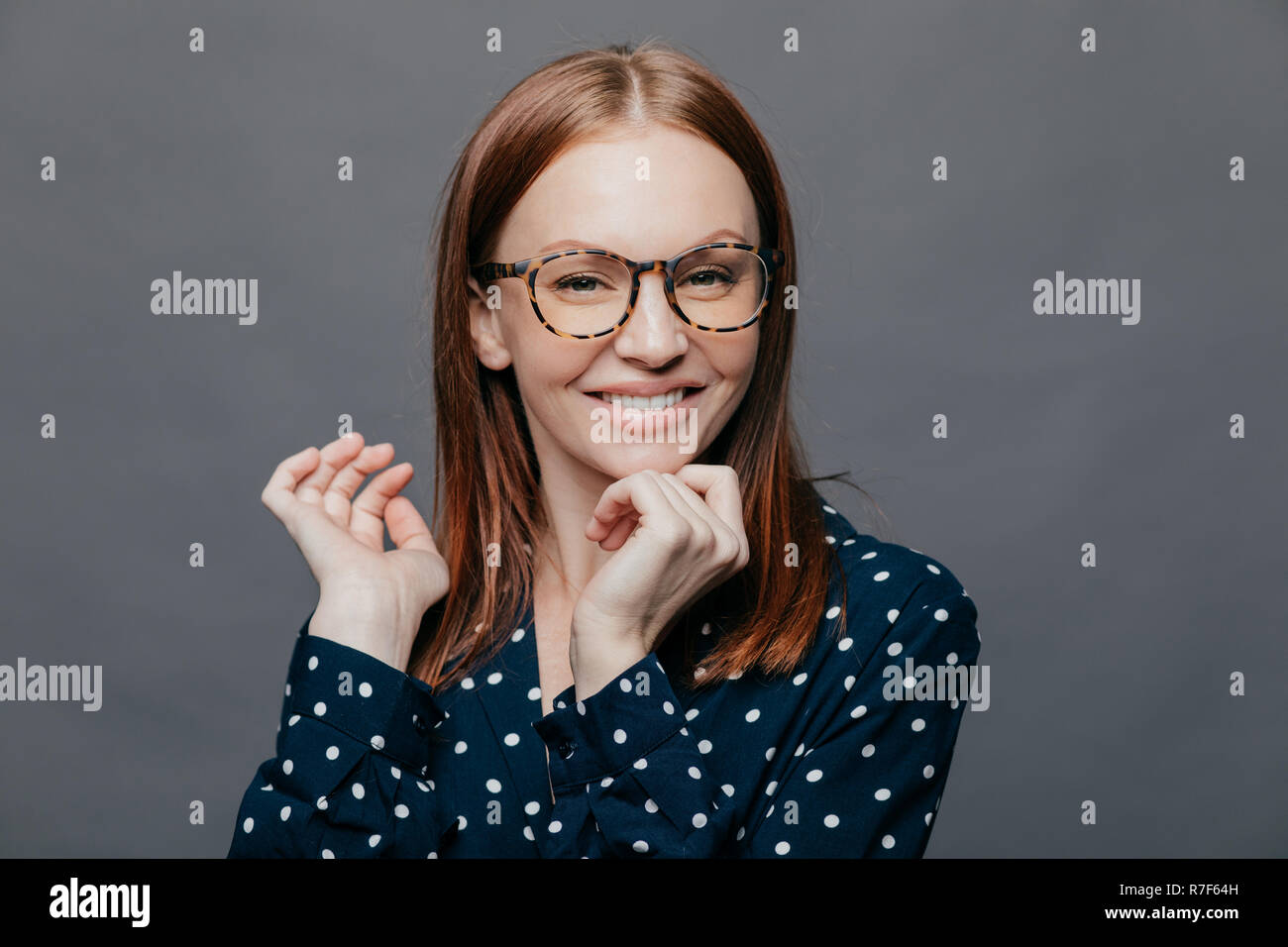 Positive attractive Caucasian woman keeps hand near chin, looks ...