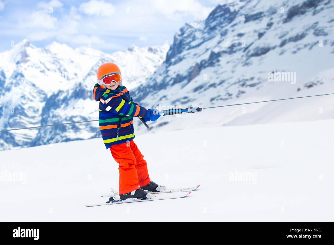 Child on a button ski lift going uphill in the mountains on a sunny ...