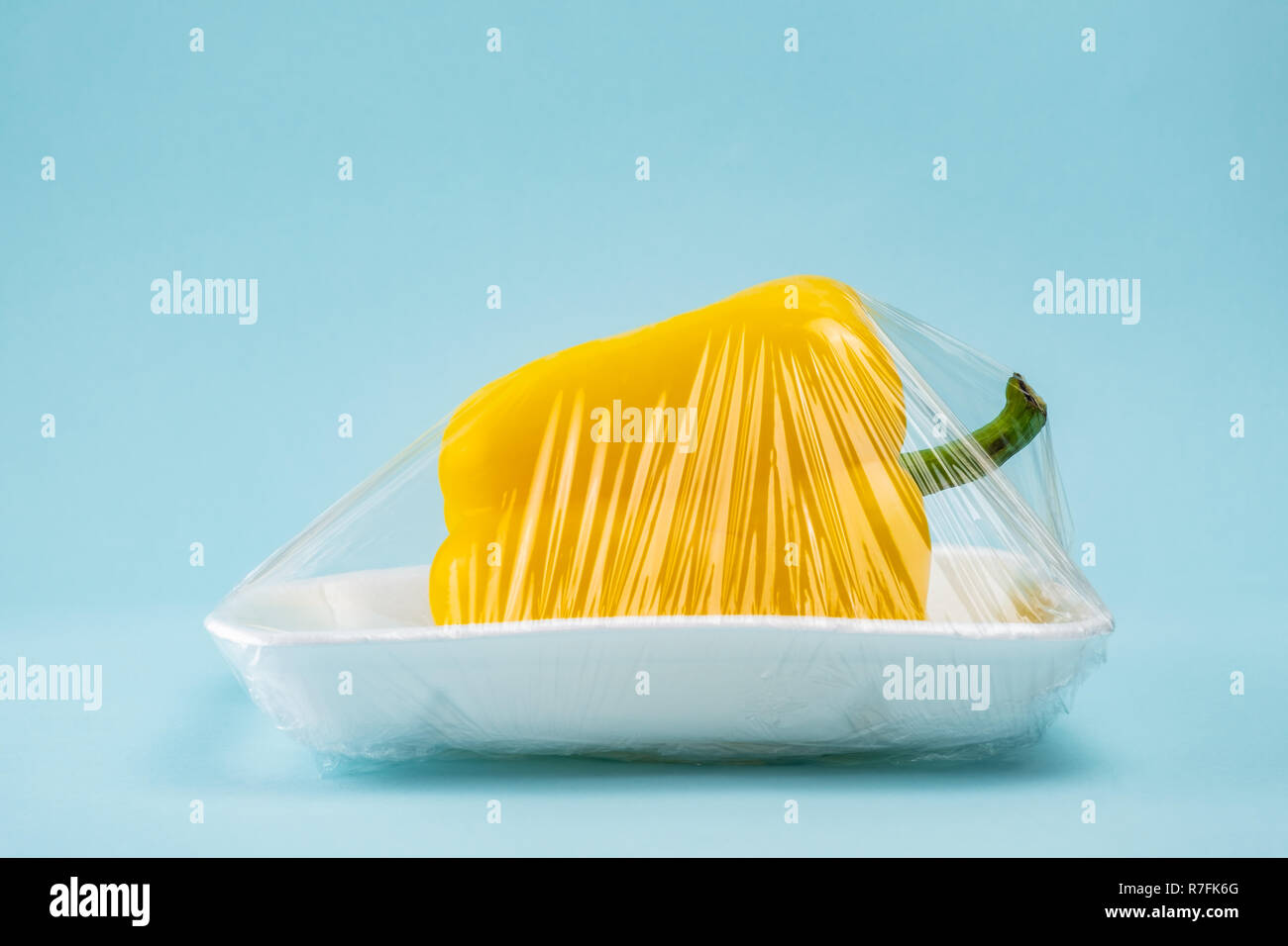 Yellow bell pepper wrapped in plastic clingfilm in blue background ...