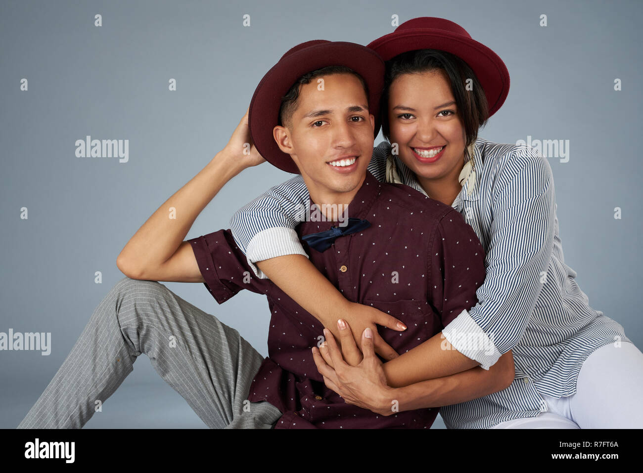 Young latin hipsters couple sit on gray studio background Stock Photo ...