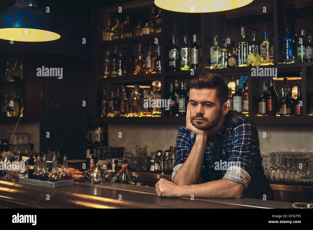 Young bartender leaning on bar counter thoughtful Stock Photo - Alamy