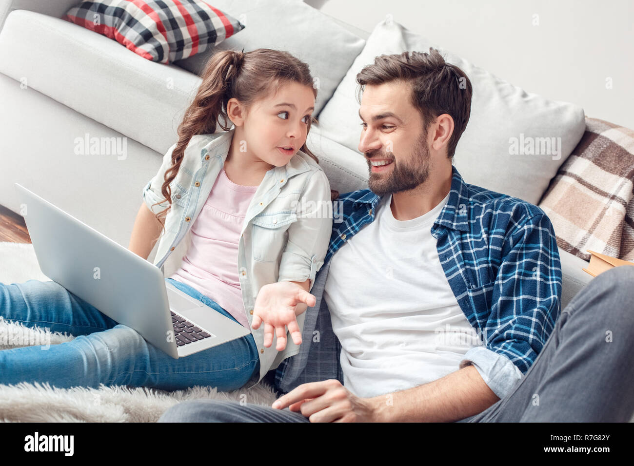 Father and little daughter at home sitting girl with laptop looking at ...