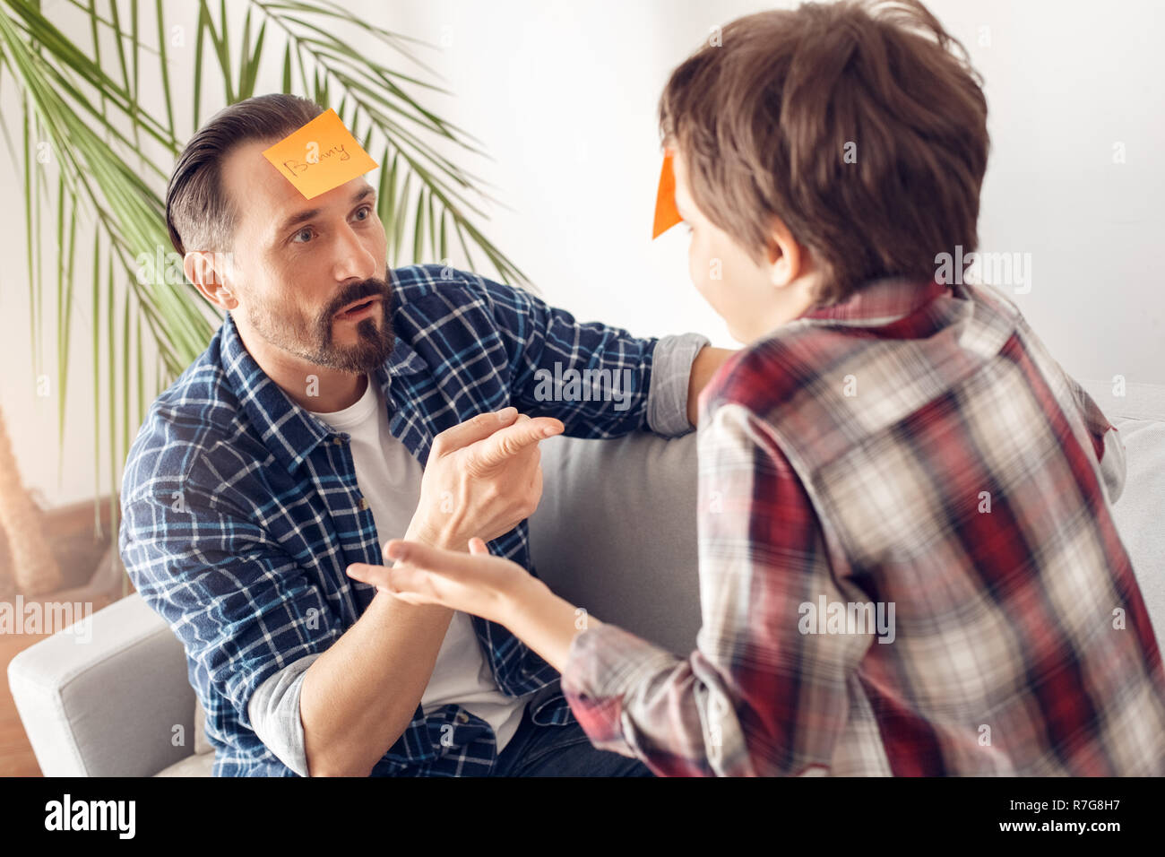 Father and little son at home sitting on sofa playing forehead ...