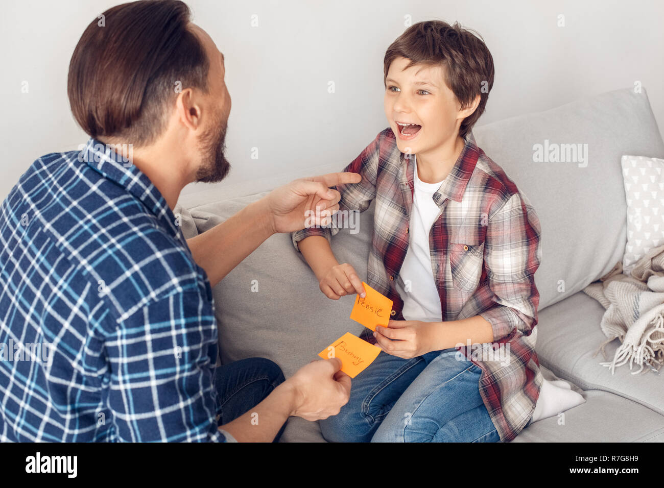 Father and little son at home sitting on sofa playing forehead ...