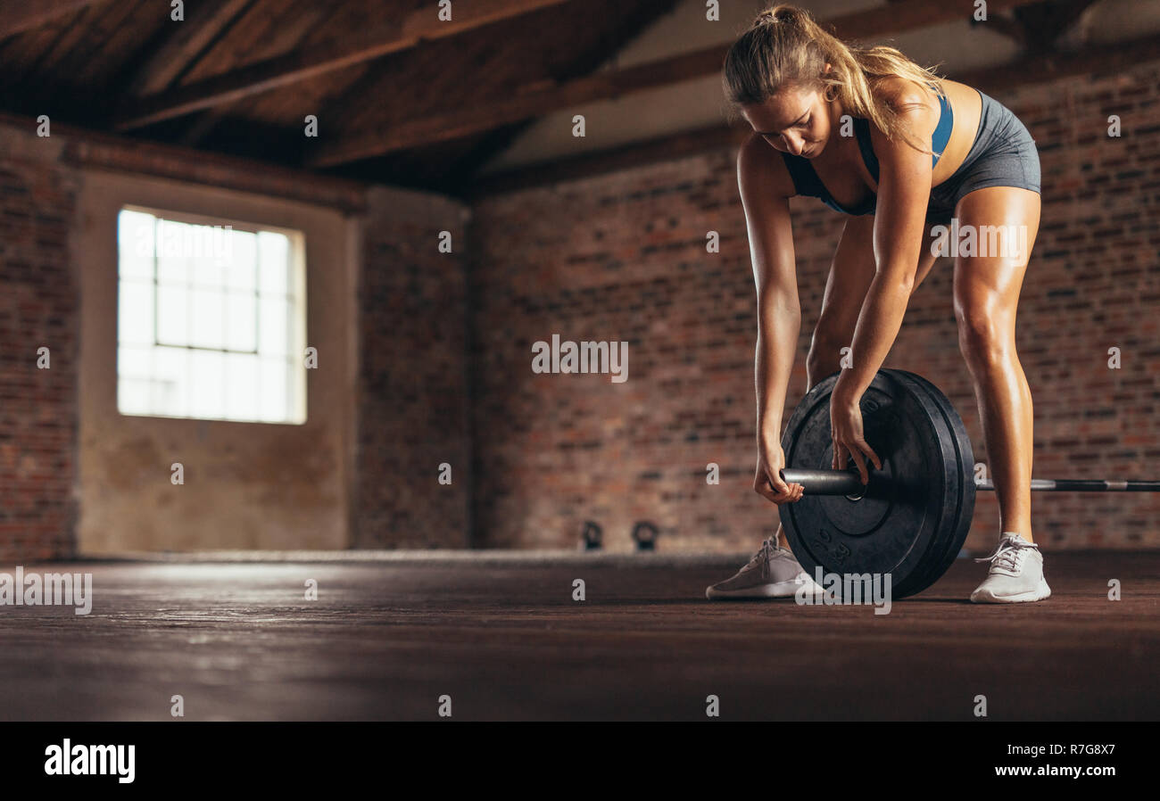 Female athlete preparing weights for exercising at fitness club ...