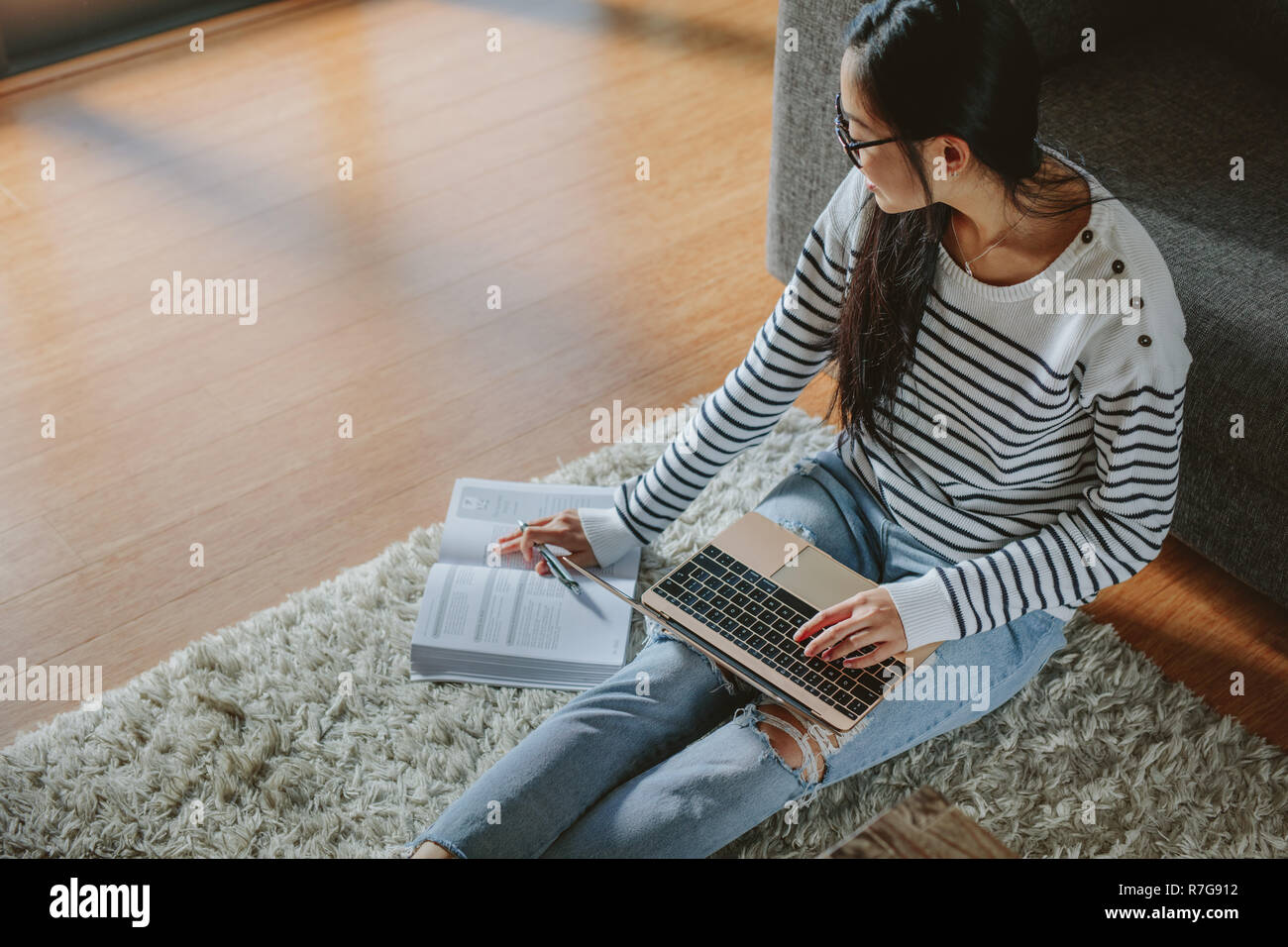 Top view of woman sitting on floor and studying with book and laptop ...
