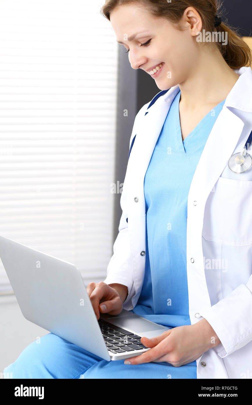 Woman doctor typing on laptop computer while working in hospital office ...