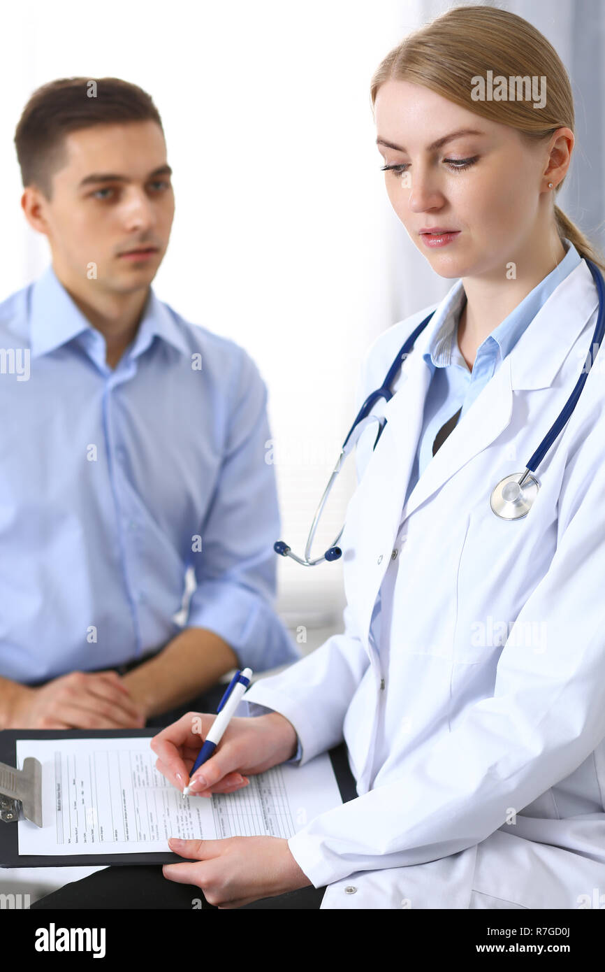 Female doctor holding application form while consulting man patient in ...