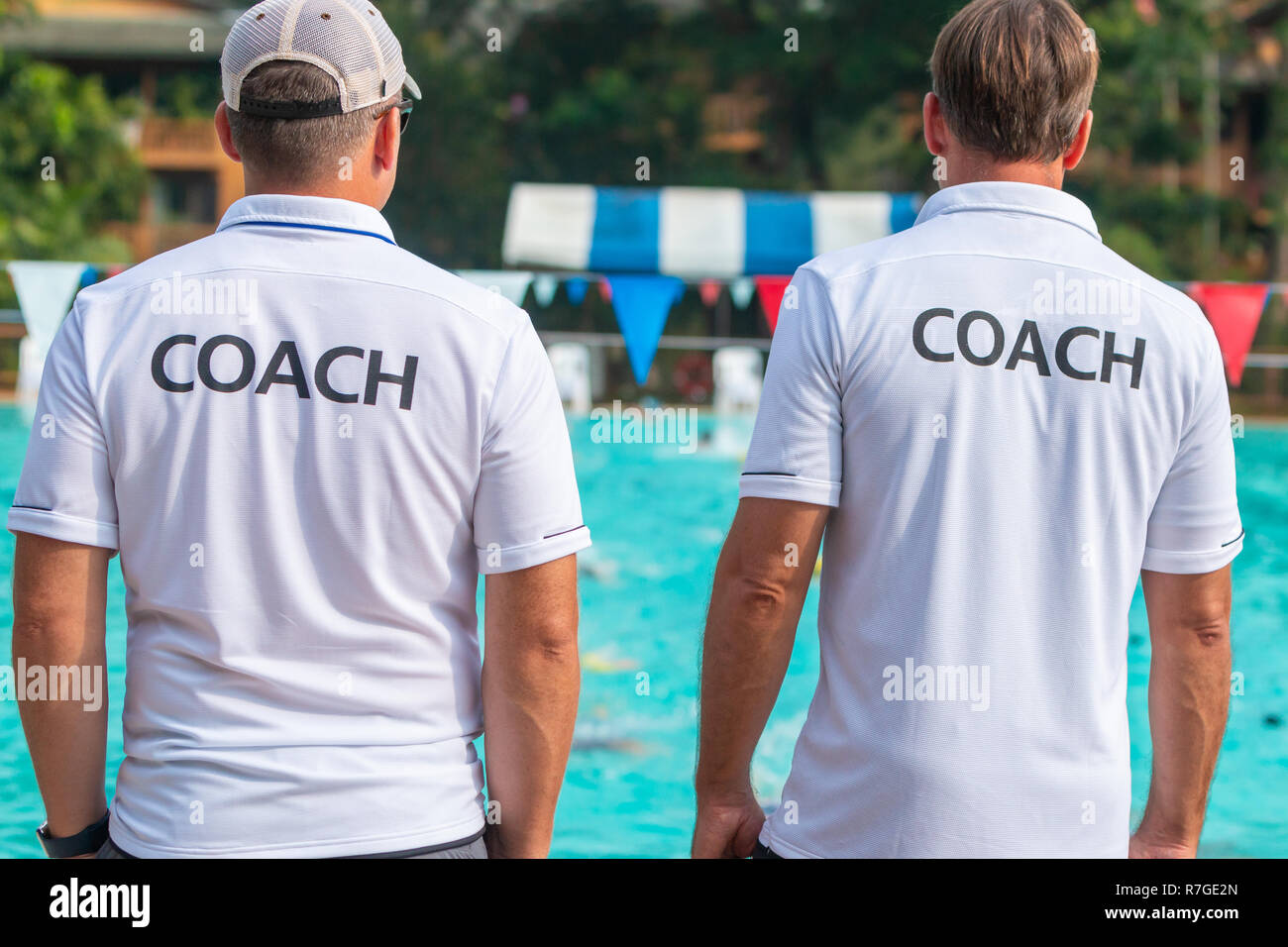 Back View Of Swimming Coaches Wearing Coach Shirt Working Together At