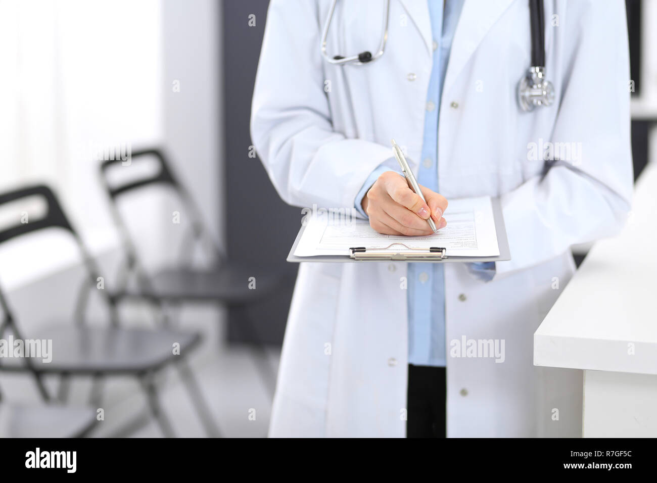Doctor woman filling up medical form while standing near reception desk ...