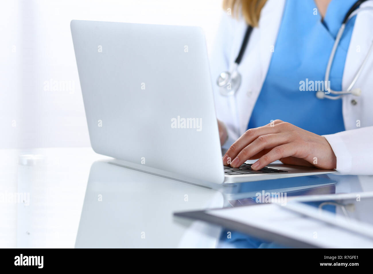 Doctor typing on laptop computer while sitting at the glass desk in ...