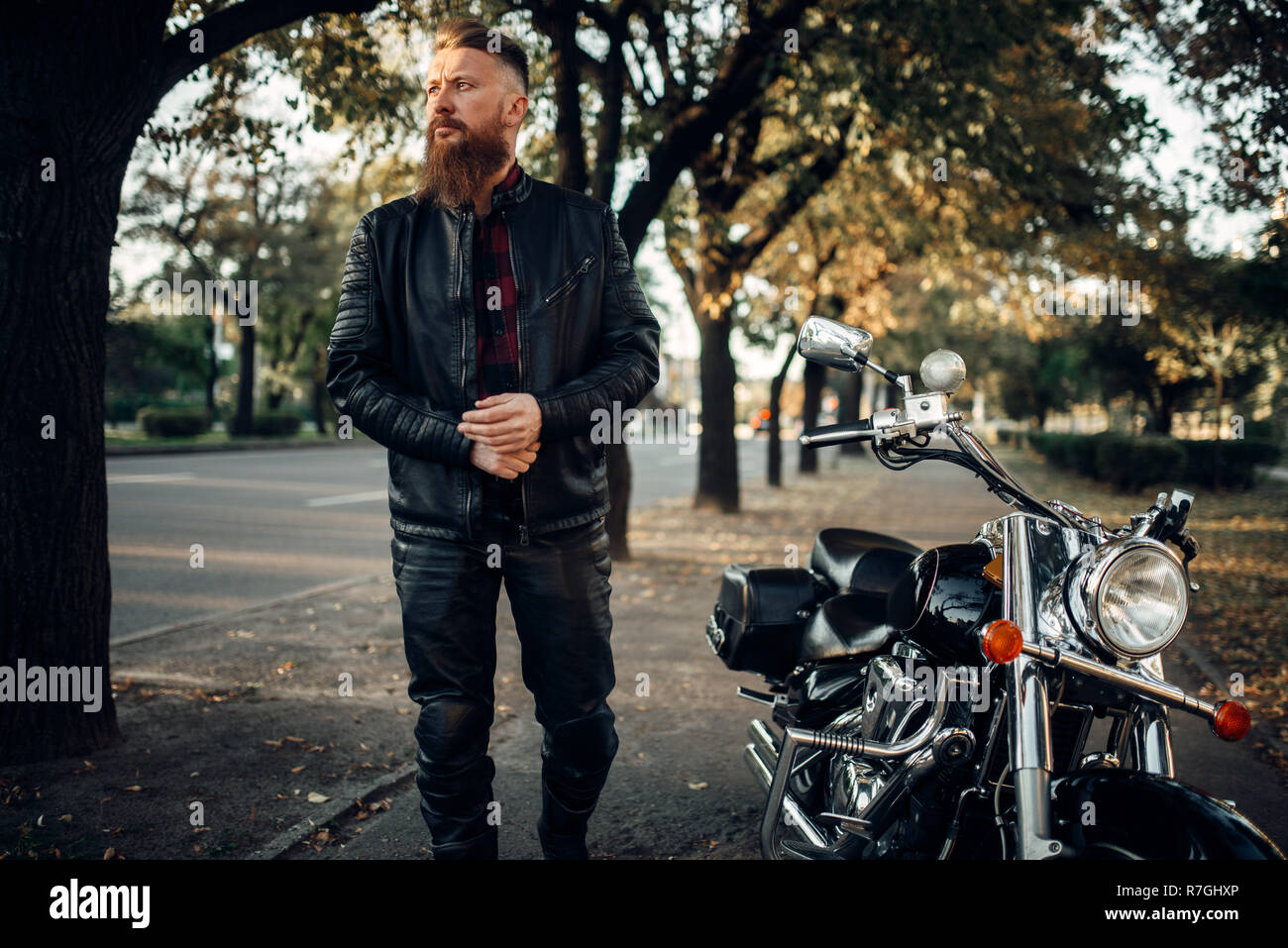 Biker in leather jacket standing near black chopper. Vintage bike ...